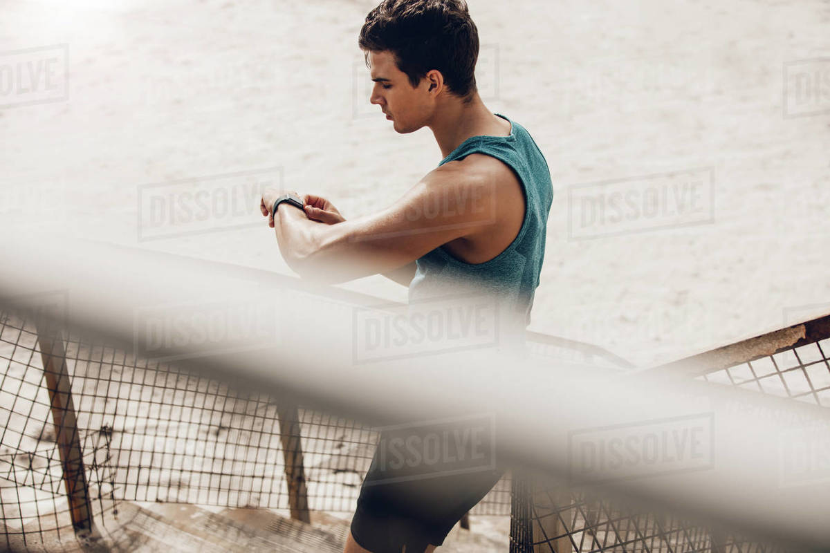 Young man standing outdoors using a smartwatch to monitor his progress ...