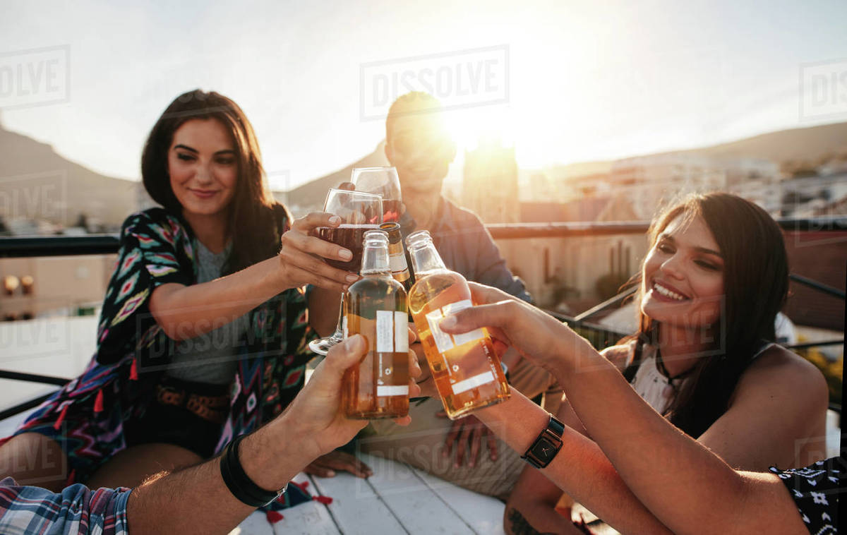 Friends toasting drinks on a rooftop. Group of friends hanging out ...
