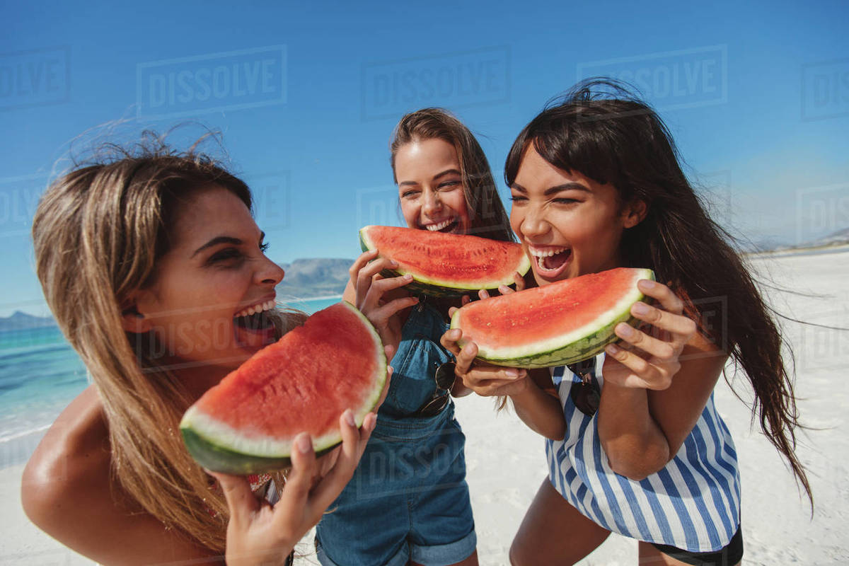 Portrait of young female friends laughing and eating watermelon on the ...