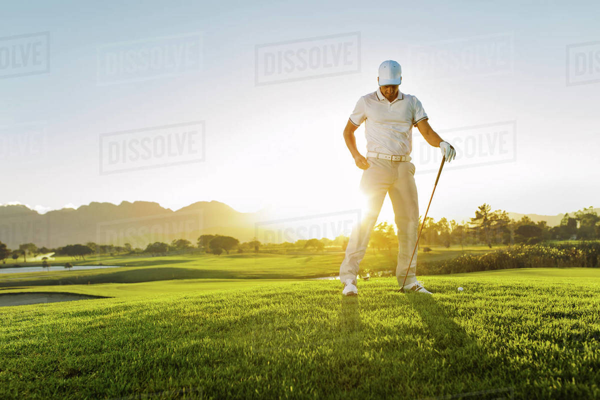 Full length of young man standing on golf course at sunset ...