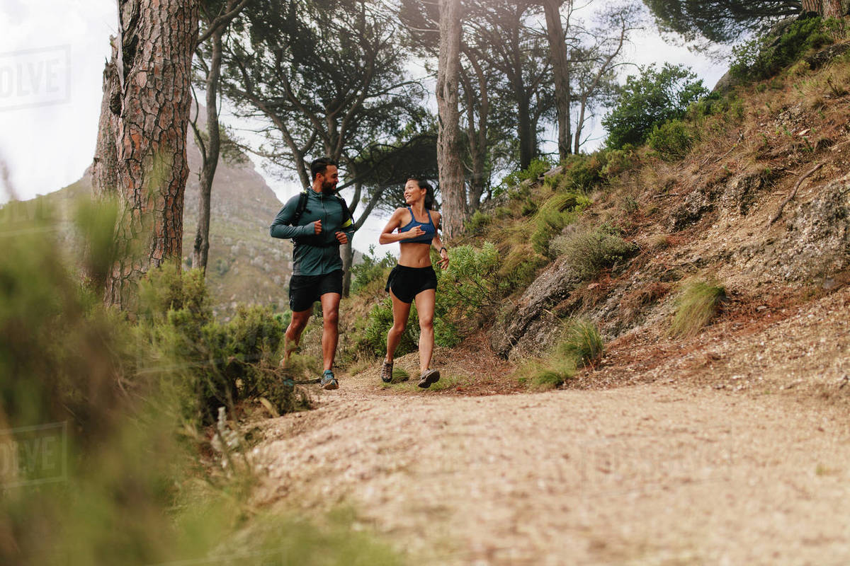 Full length portrait of young man and woman running on country path ...