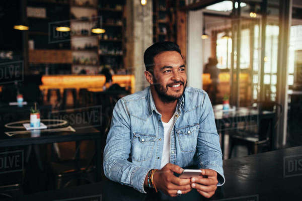 Indoor shot of young man sitting in coffee shop with mobile phone ...