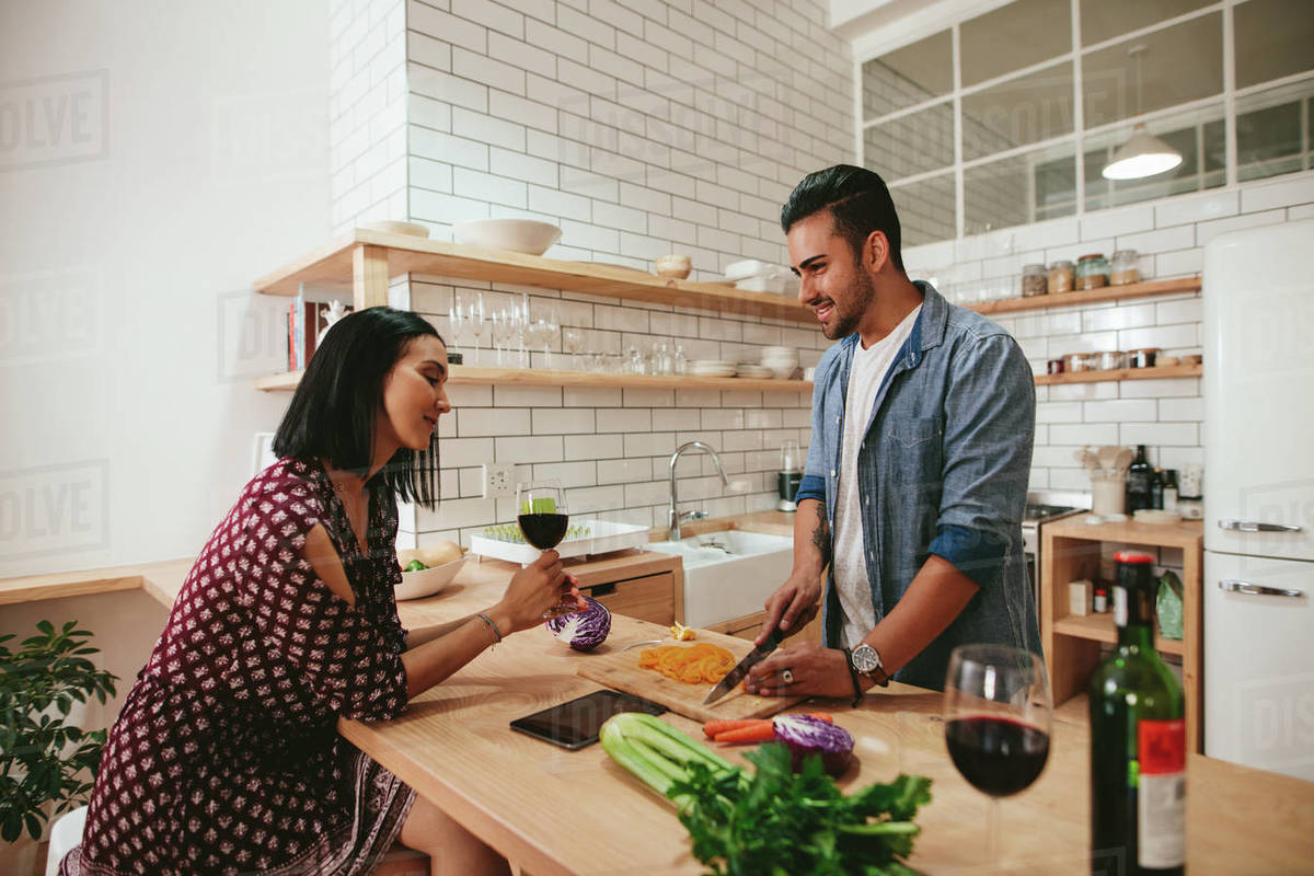 Young couple talking while cooking in kitchen at home. Young woman ...