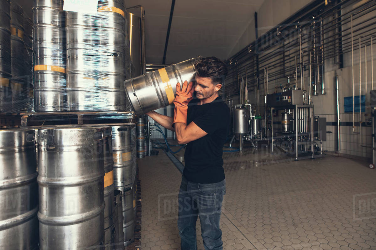 Young male brewer with keg at brewery factory warehouse. Young man ...