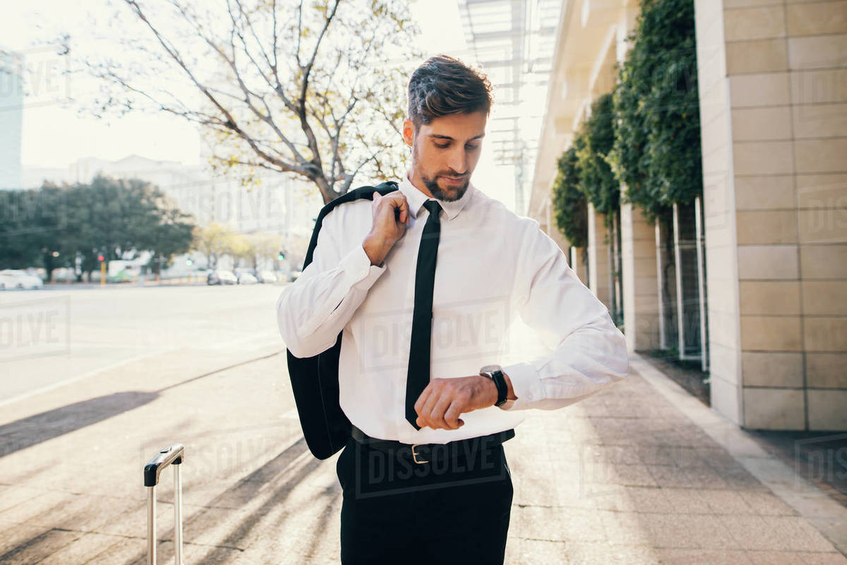 Handsome young man walking outside on the city street and checking time ...