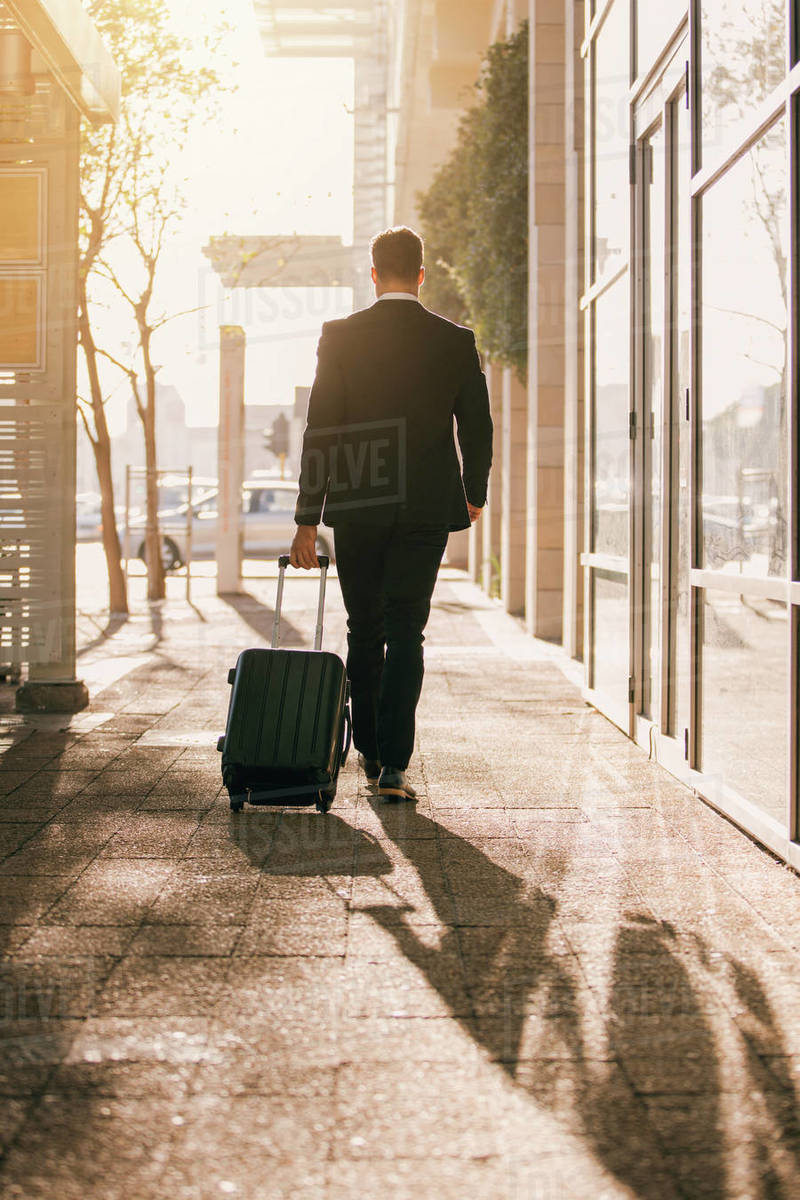 Vertical shot from behind of man walking with bag outside on city ...