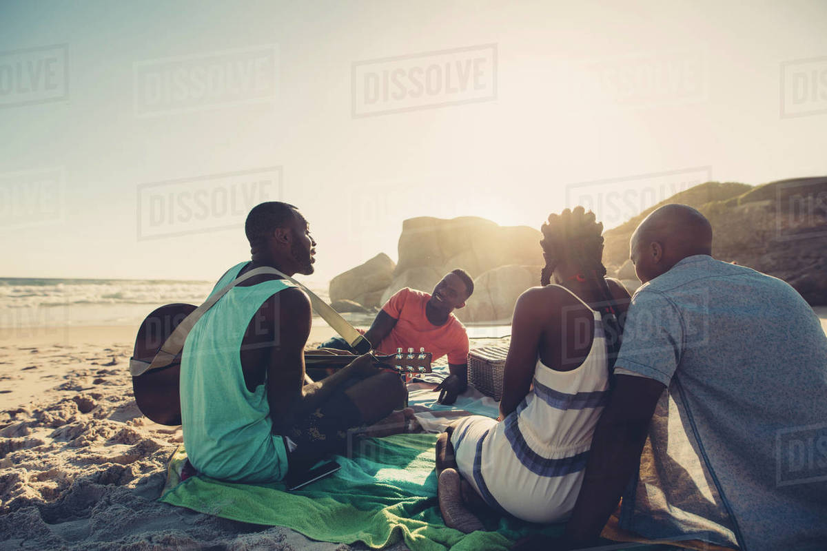 African young man singing and playing guitar on the beach. Group of ...