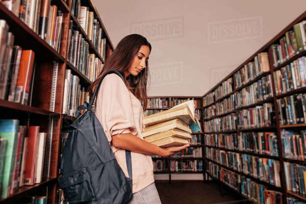 Young female student carrying lots of books in the college library ...