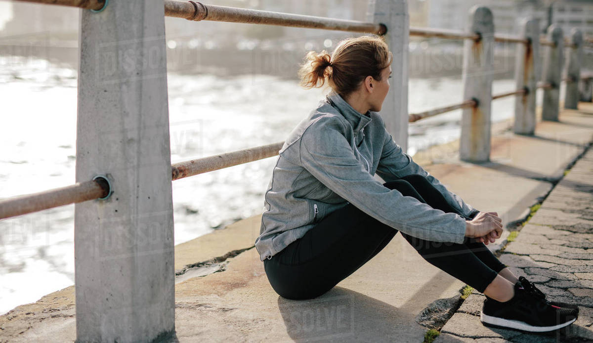 Woman runner sitting at seaside promenade after workout. Woman sitting ...