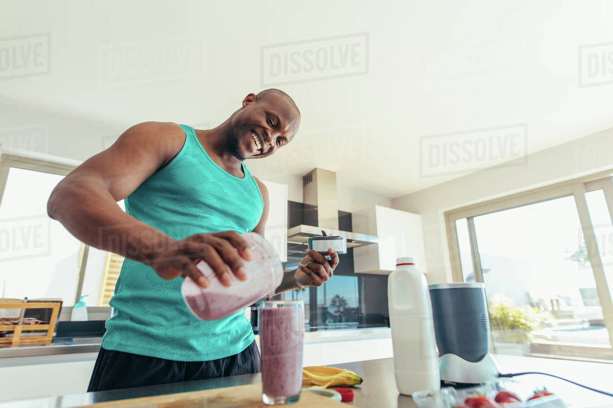 Man preparing milk shake in kitchen. Smiling man pouring milkshake in a ...
