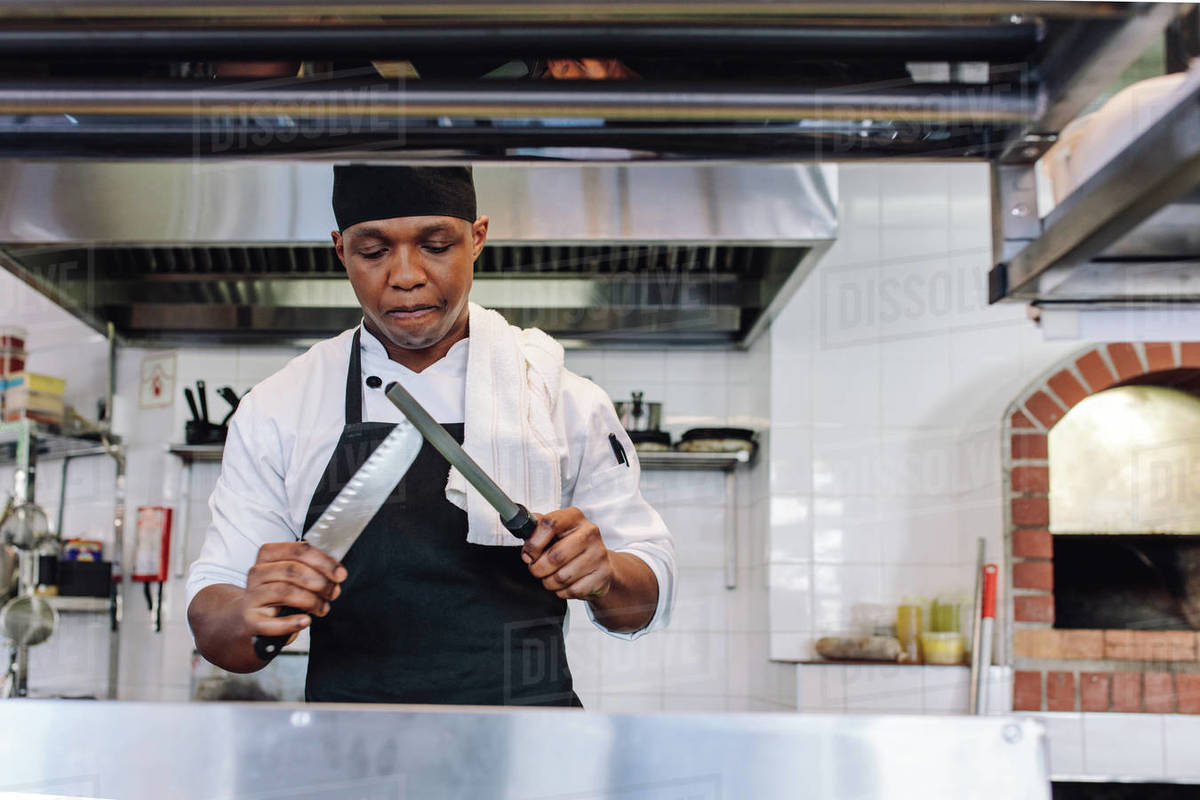 African male chef sharpening his knife at restaurant kitchen. Cook ...