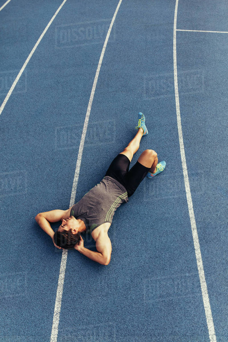 Runner lying on the track in a relaxed mood with hands under his head ...