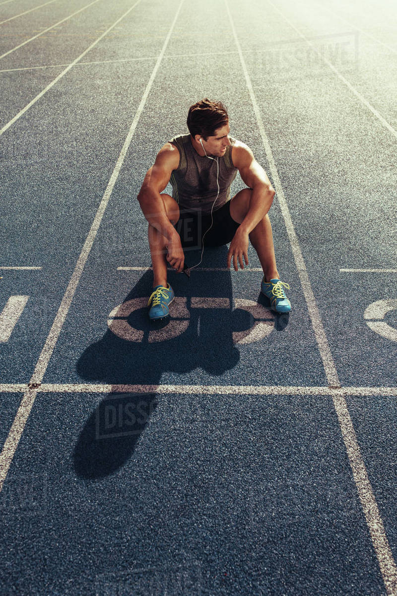 Athlete sitting on a running track listening to music. Runner wearing ...