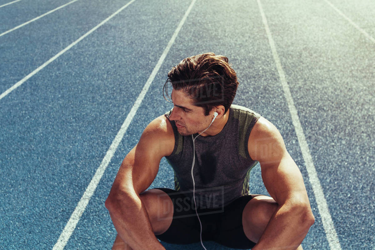 Close up of an athlete sitting on a running track listening to music ...
