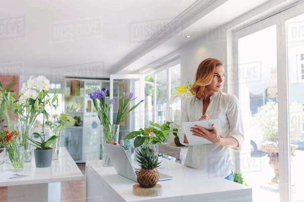 Woman florist working in flower shop with clipboard and looking outside ...