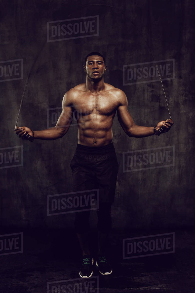 Bare chested man skipping at the gym. Muscle athlete working out with a ...