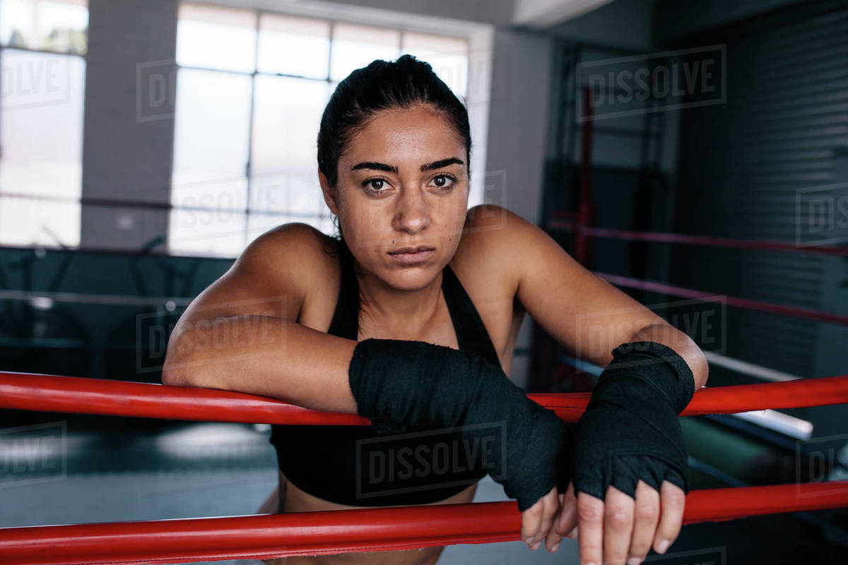 Female boxer standing inside a boxing ring. Boxer resting her arms on ...