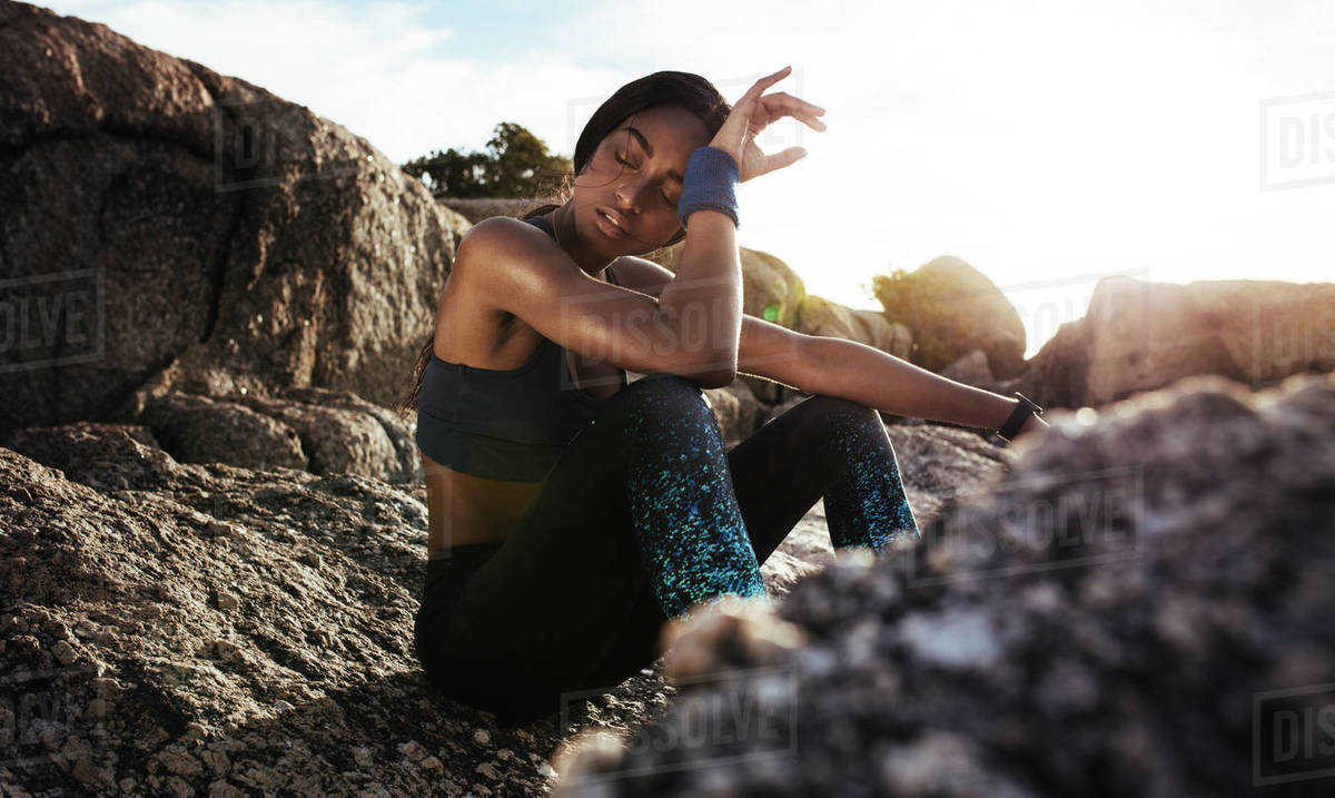 Tired woman sitting and resting after workout on rocks. Woman feeling ...
