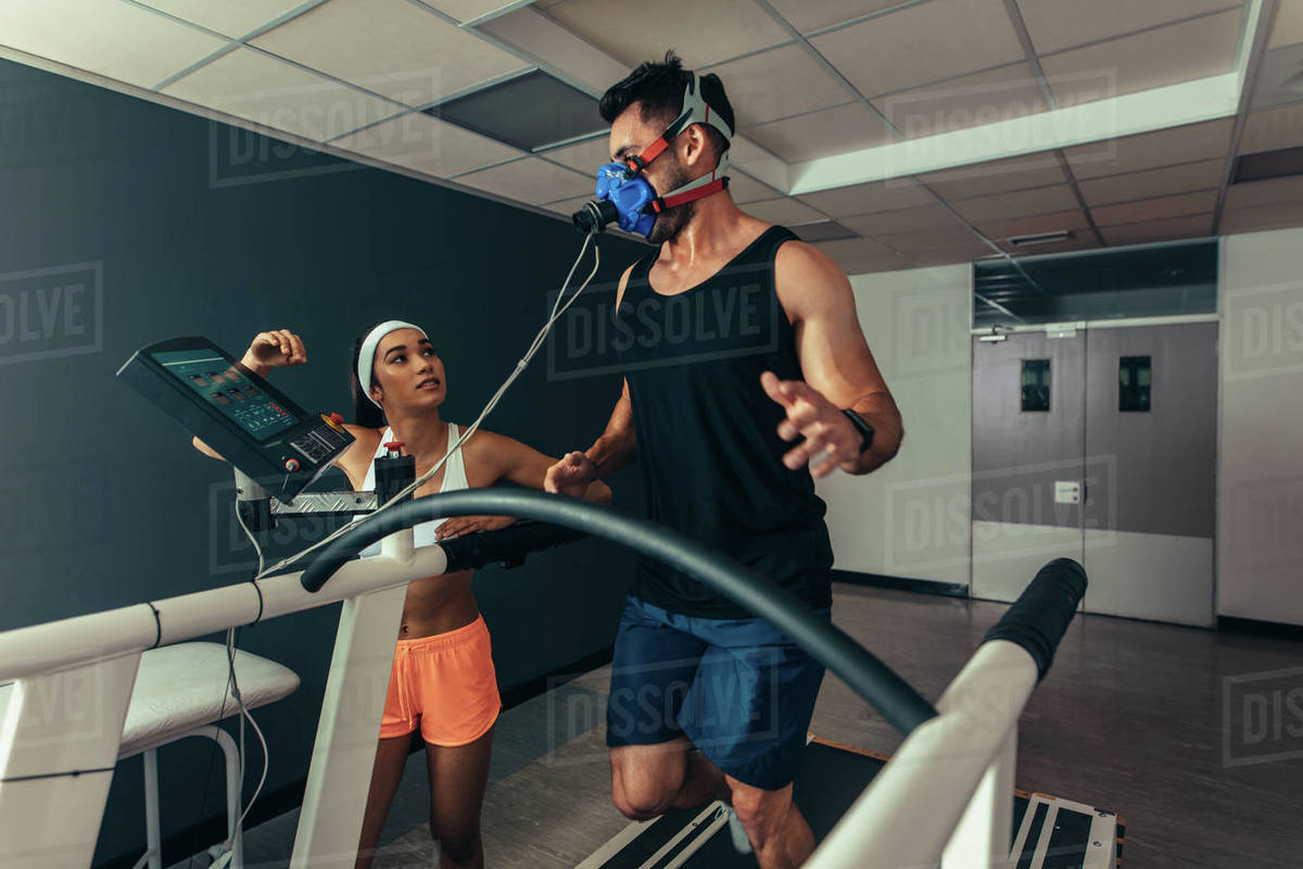 Runner with mask on treadmill in laboratory with woman standing by ...