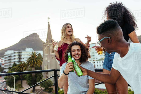Happy young men toasting beers with girls laughing and enjoying at the ...