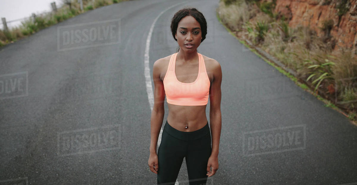 Closeup of woman athlete standing on empty road. Runner posing during ...