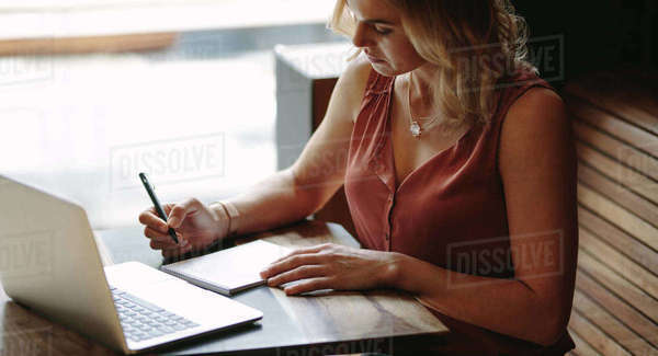Freelancer writing notes sitting at a coffee table. Woman working on ...