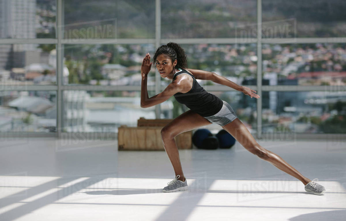 Portrait of fit young african woman standing in gym with stretching ...
