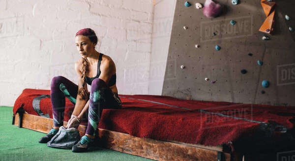 Woman at a wall climbing gym applying magnesium chalk powder on hands ...
