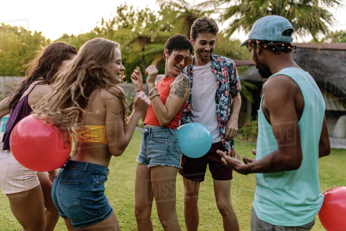 Group of men and women playing balloon bursting game during a party ...
