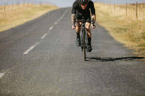 Athlete riding bicycle on empty road. Cyclist rides his bike through ...