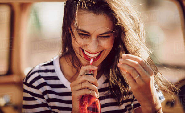 Closeup of beautiful young woman drinking soda with straw from a glass ...