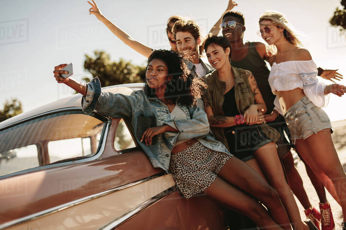 Group of young people on a road trip standing together by the car and ...