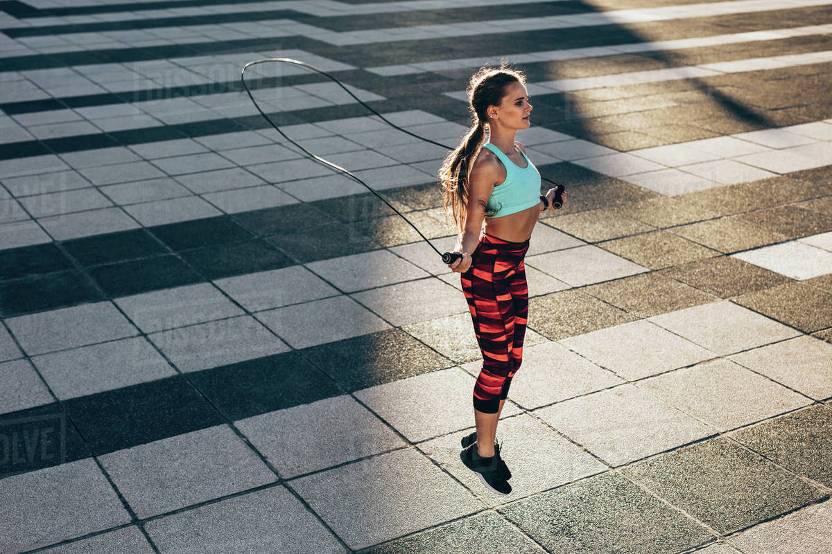 Full length of sportswoman jumping ropes in morning. Fit athlete ...