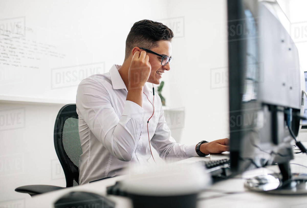 Smiling software developer sitting at his office desk working on laptop ...