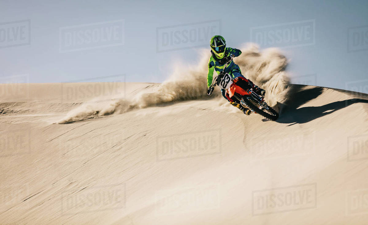Motocross rider accelerating in sand dunes with debris flying away ...
