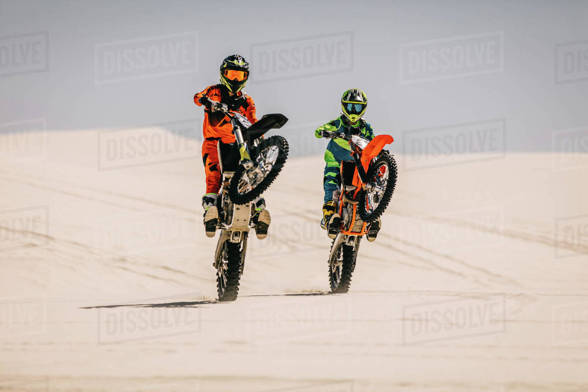 Skillful stunt bikers riding motorcycle on one wheel in desert. Two ...