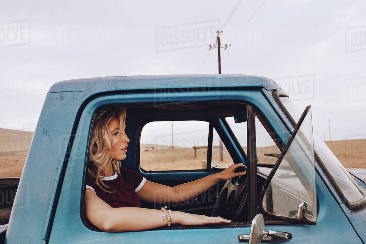 Side view of young woman driving a truck on country road. Female on a ...