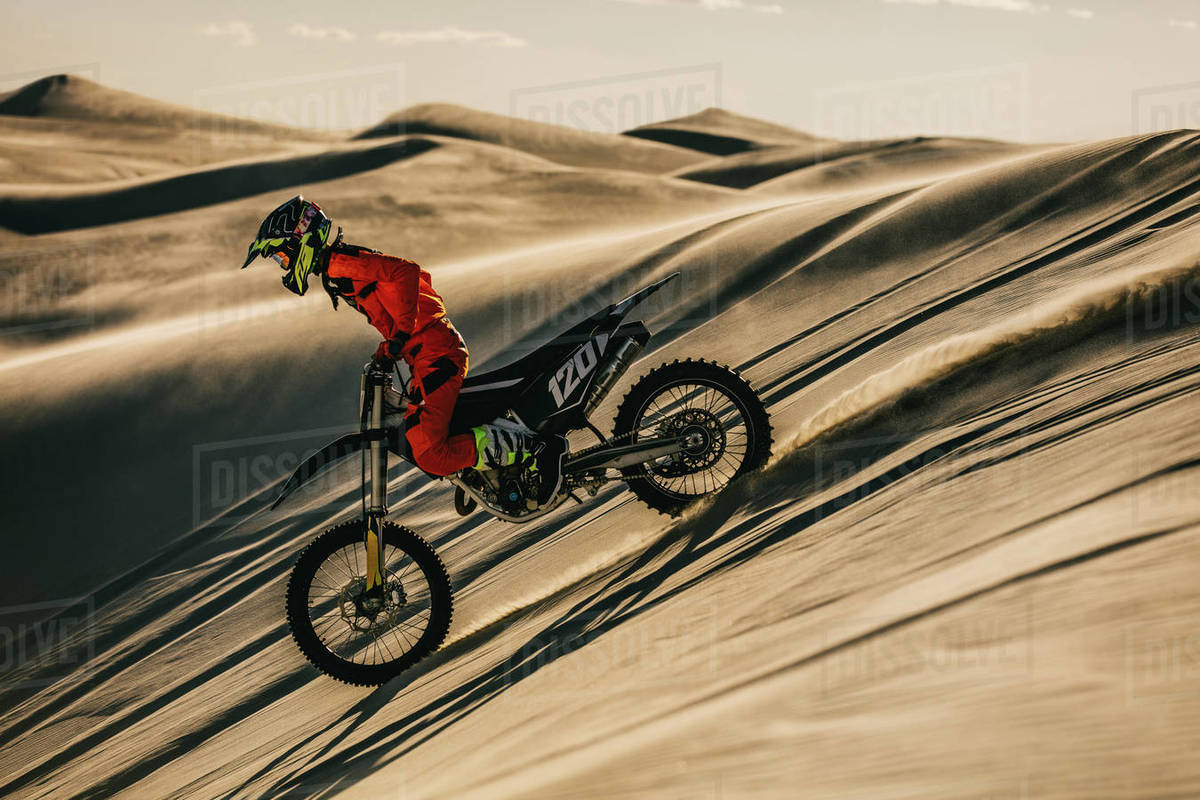 Motocross rider riding his racing bike down the sand dune. Motorbike ...
