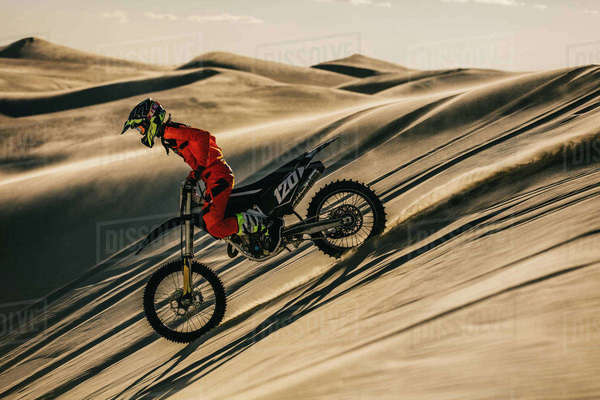 Motocross rider riding his racing bike down the sand dune. Motorbike ...