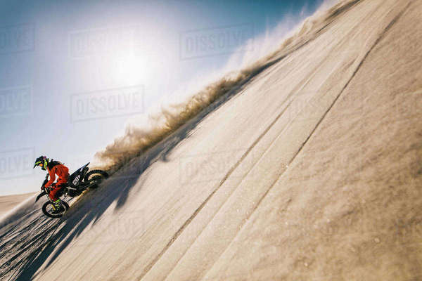 Motocross rider riding on his bike down a sand dune leaving a trail of ...