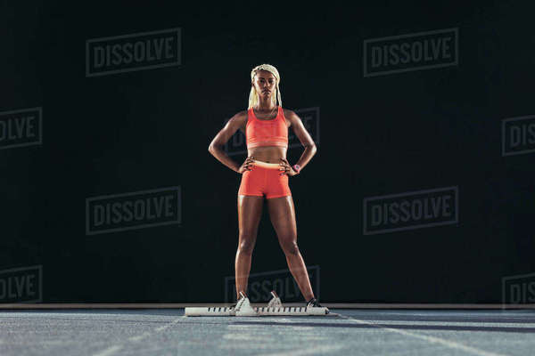 Female sprinter standing beside a starting block on running track on a ...