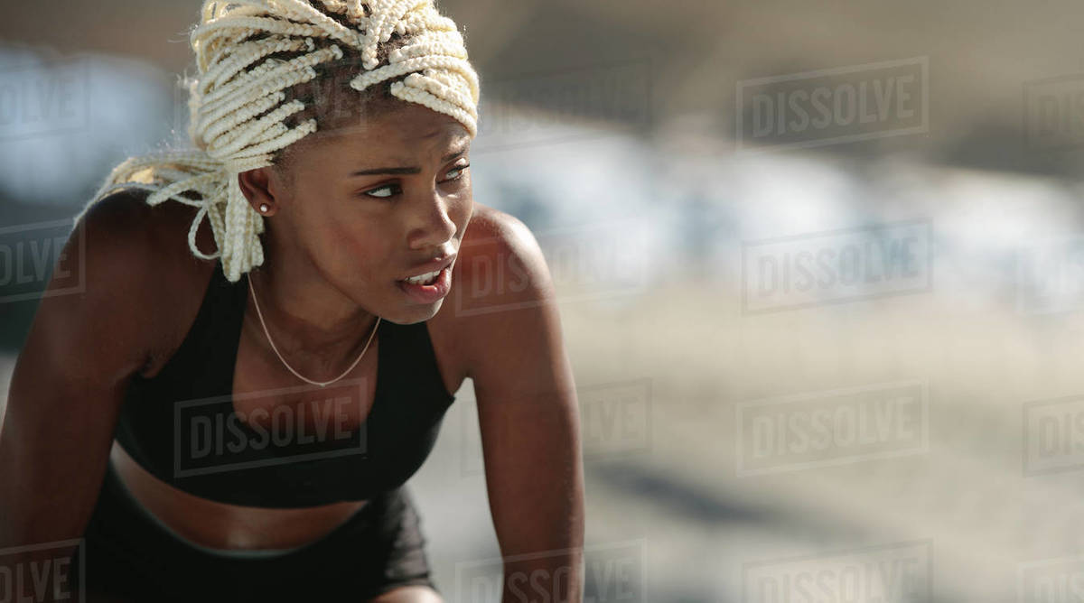 Close up of a female sprinter standing inside a stadium. Tired athlete ...