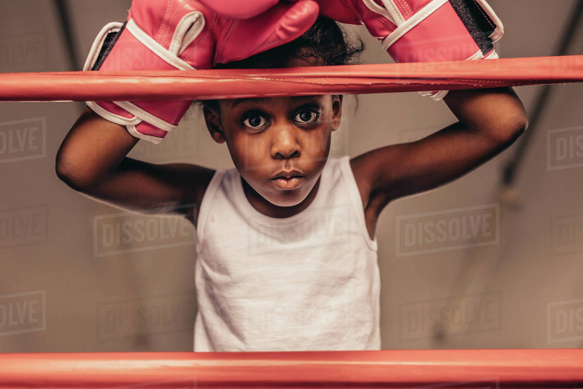 Kid wearing boxing gloves standing near a boxing ring. Close up of a ...