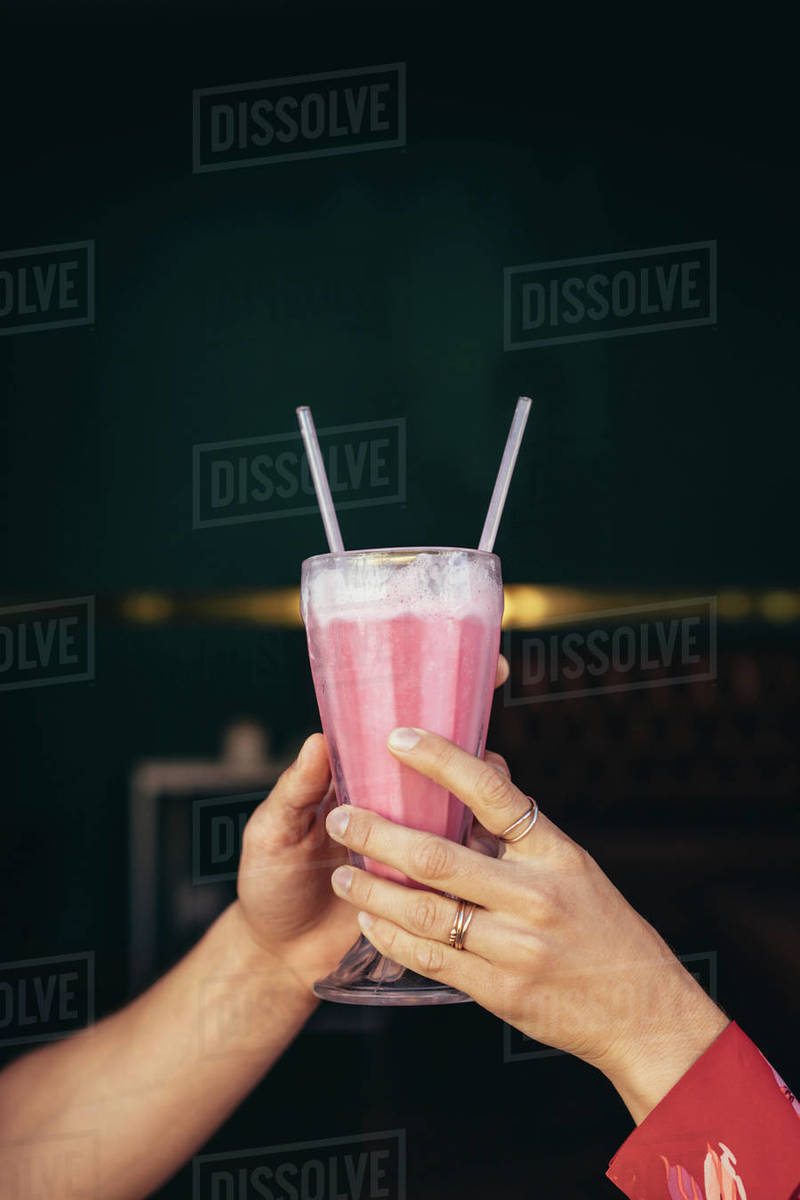 Close up of hands of a couple holding a glass of milkshake with two ...