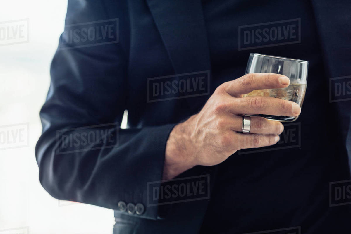 Close up of businessman hand holding a glass of whisky. Cropped shot of ...