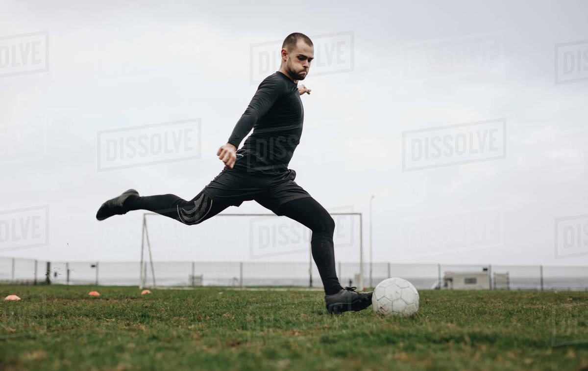Football player practicing his kicks on the field on a cloudy day. Man ...