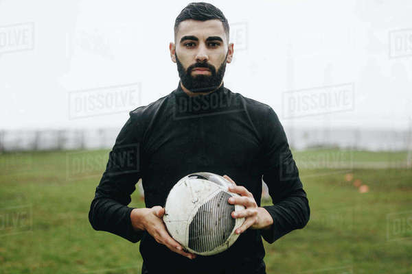 Football player standing on field holding a football in hand. Man ...