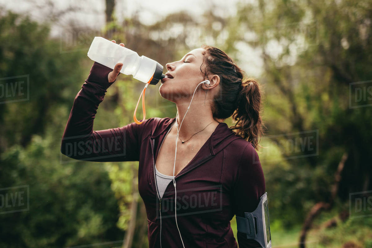 Female runner drinking water after a running working outdoors. Woman ...
