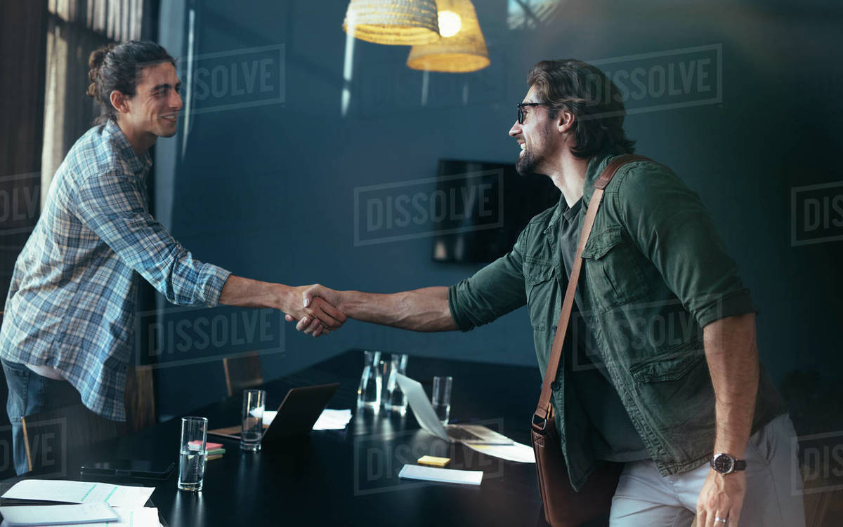 Two young man standing around the table and shaking hands. Creative ...