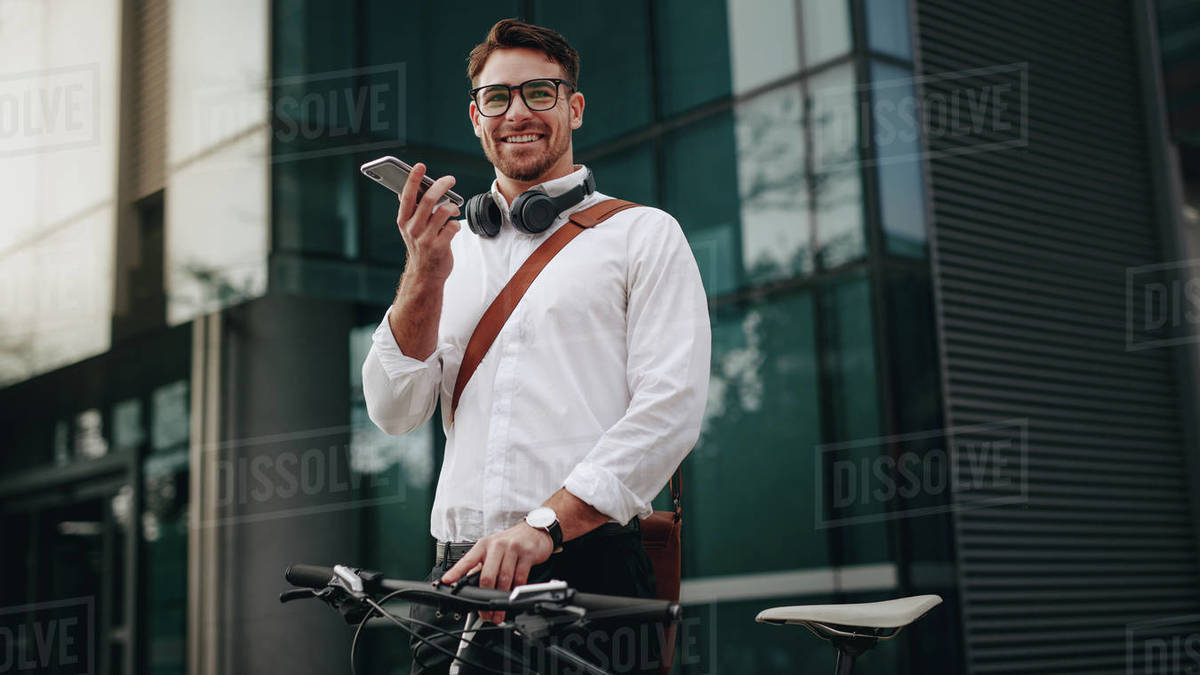 Smiling businessman talking over mobile phone standing on street with ...